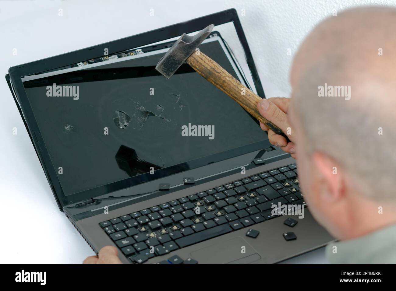 Angry man seen in profile breaking a laptop with a hammer, white ...