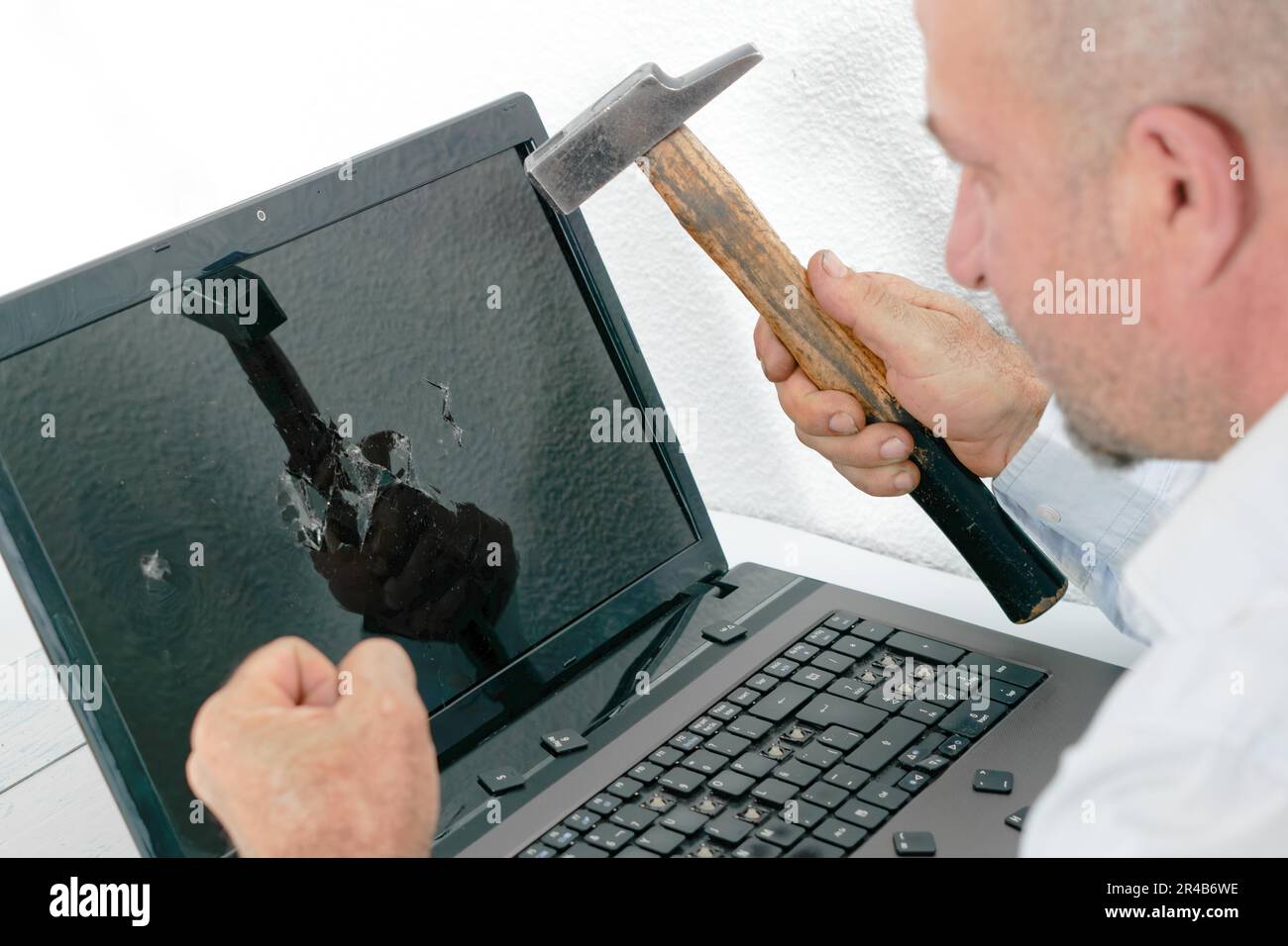 Angry man seen in profile breaking a laptop with a hammer, white ...