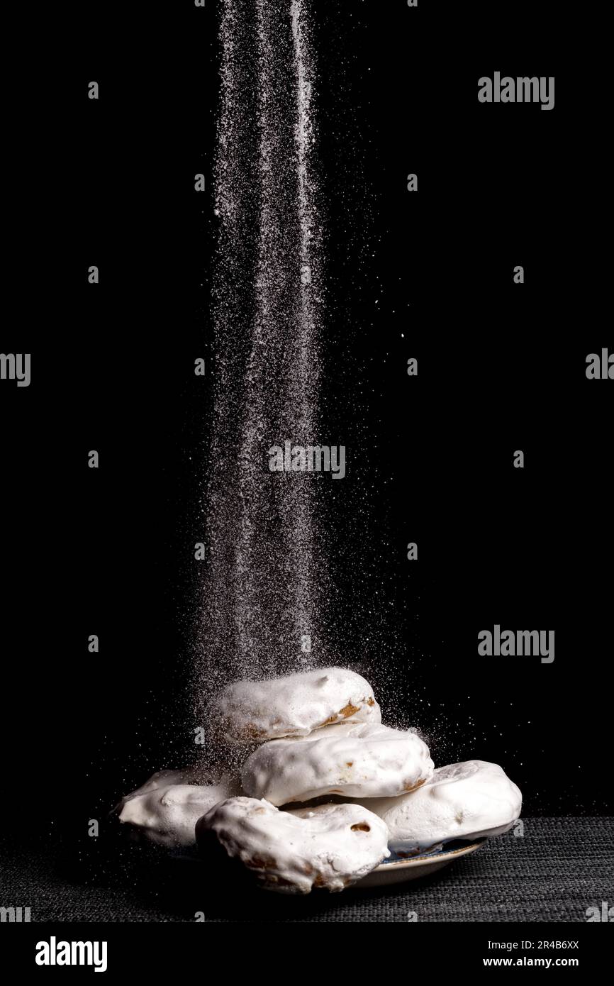 Glazed sugar doughnuts with icing sugar falling on them with black ...