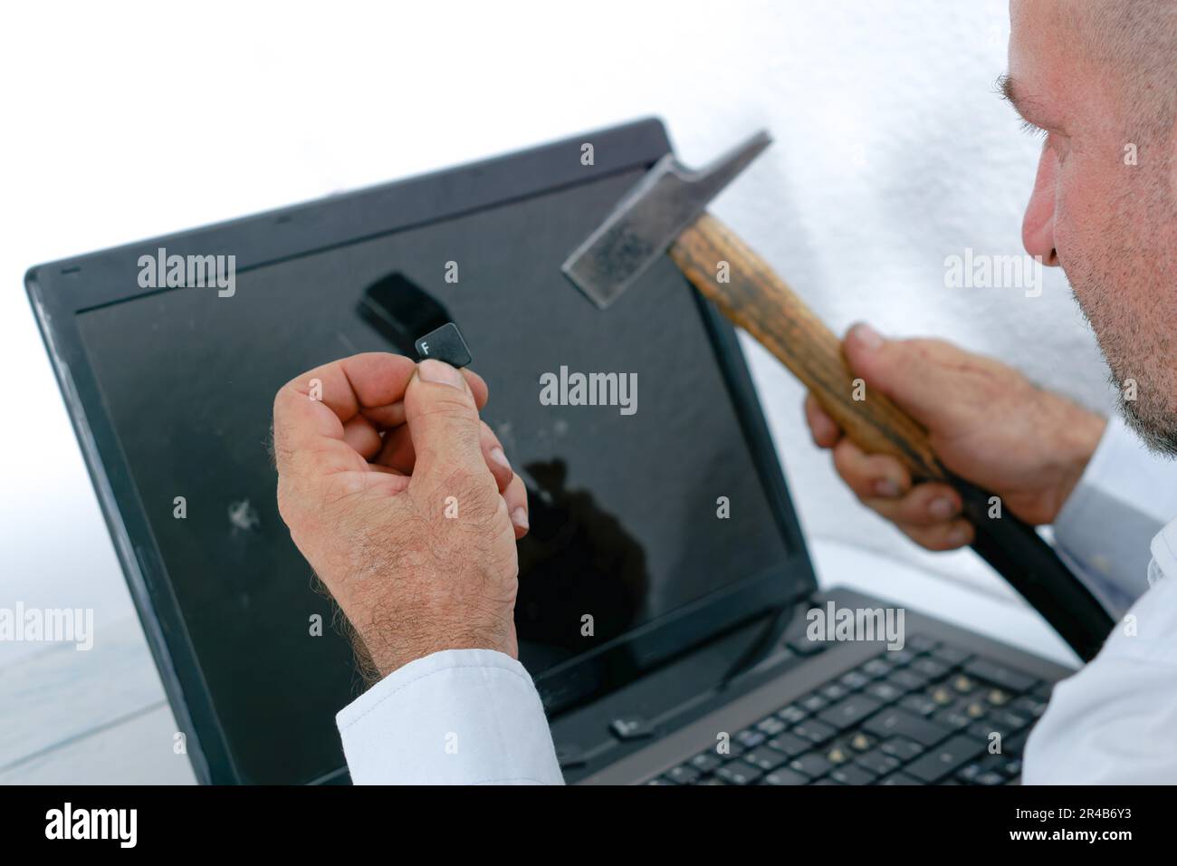 Angry man seen in profile breaking a laptop with a hammer, white ...