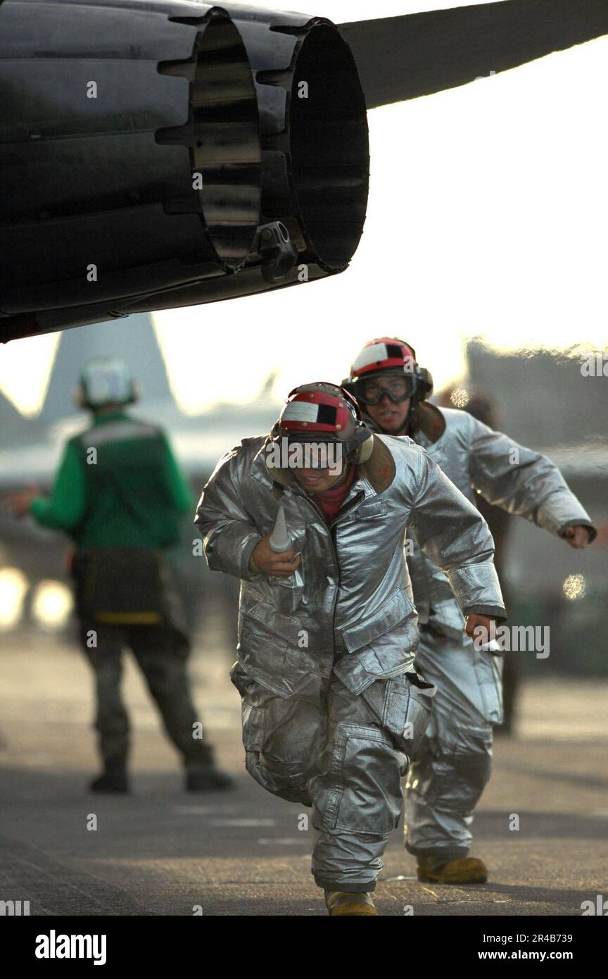 US Navy Crash and salvage personnel duck under the jet exhaust of an F ...