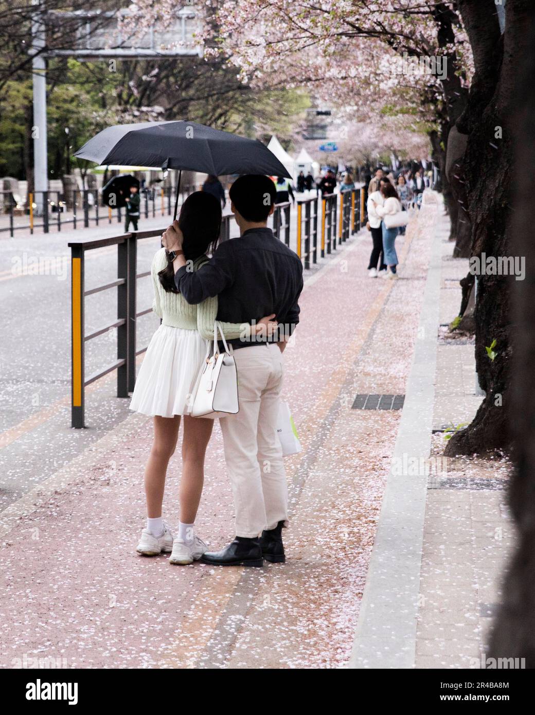 Couple with umbrella standing on the street taking a photo of ...