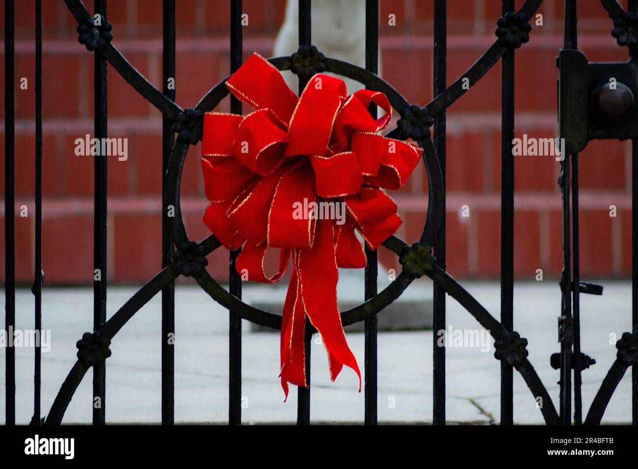 A red ribbon is tied to a wrought-iron gate on a pedestrian sidewalk ...