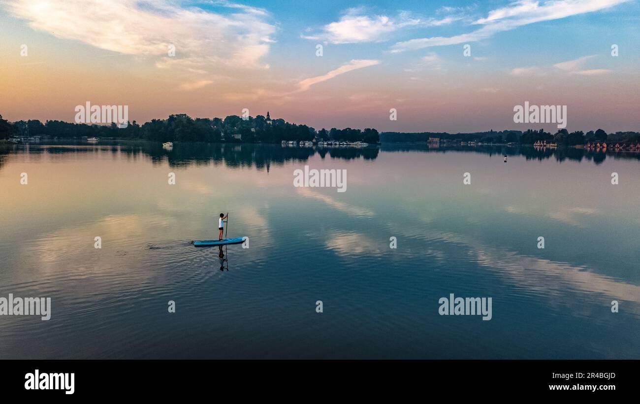 Woman paddling on SUP board on beautiful lake during sunset or sunrise ...