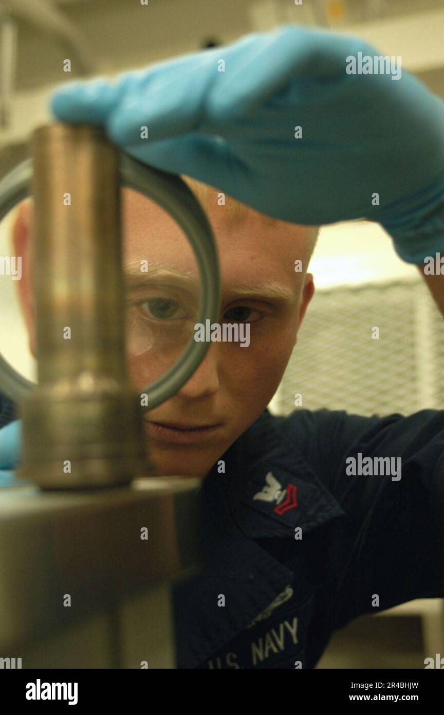 US Navy Hull Maintenance Technician 2nd Class inspects a cuplink pipe ...