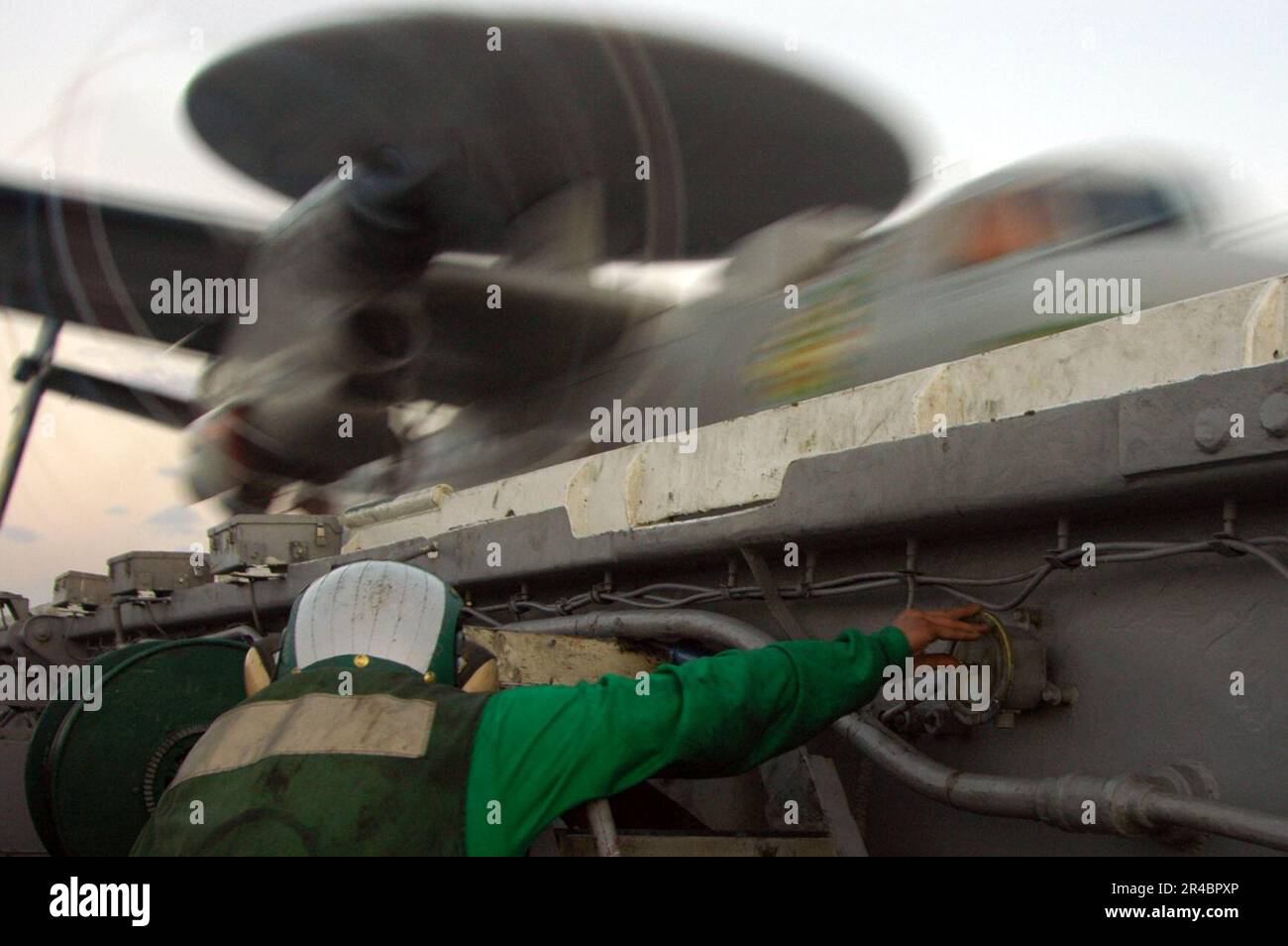 US Navy Aviation Boatswain's Mate 3rd Class ducks while an E-2C Hawkeye ...