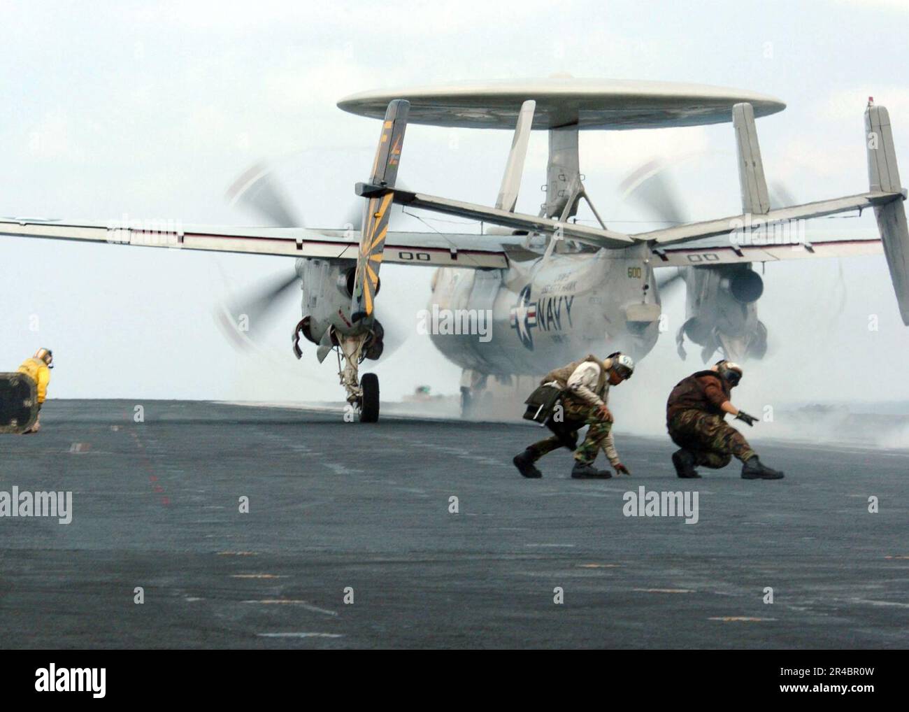 US Navy Two Sailors duck to avoid the engine blast of an E-2C Hawkeye ...