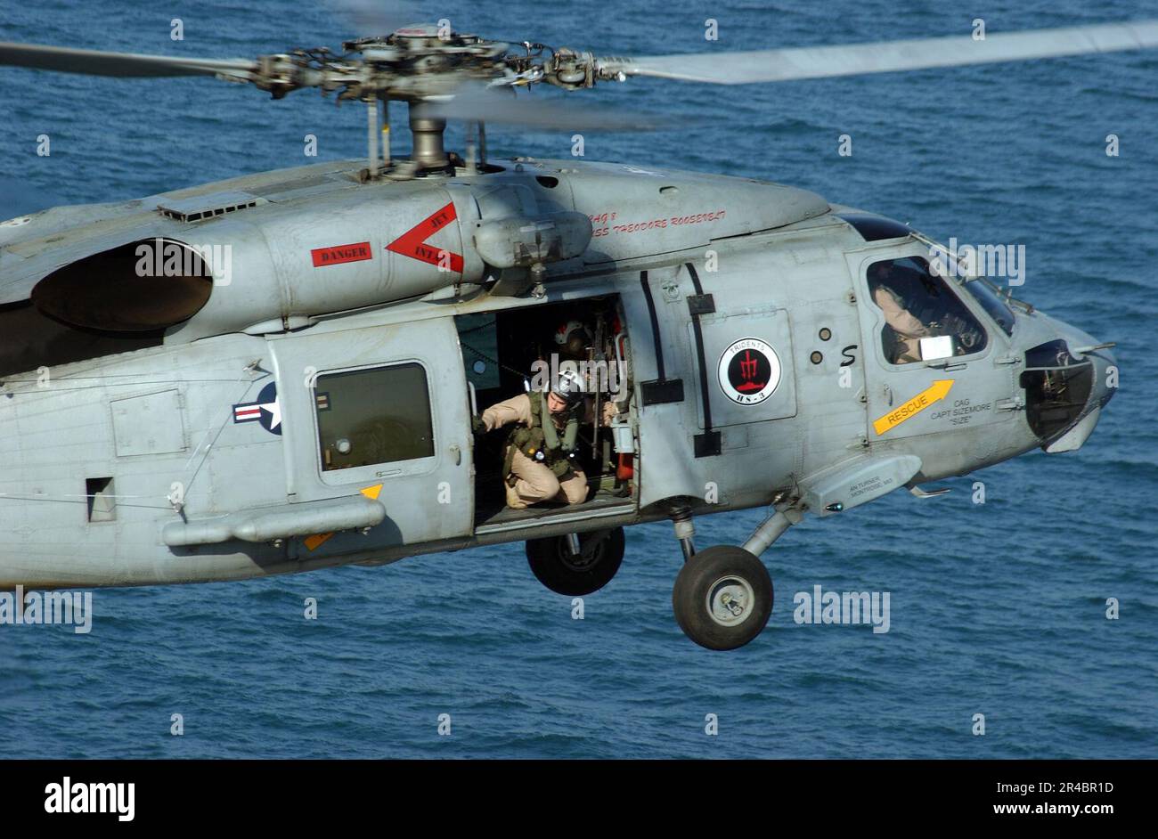 US Navy An air crew member looks out from the open door of an SH-60F ...