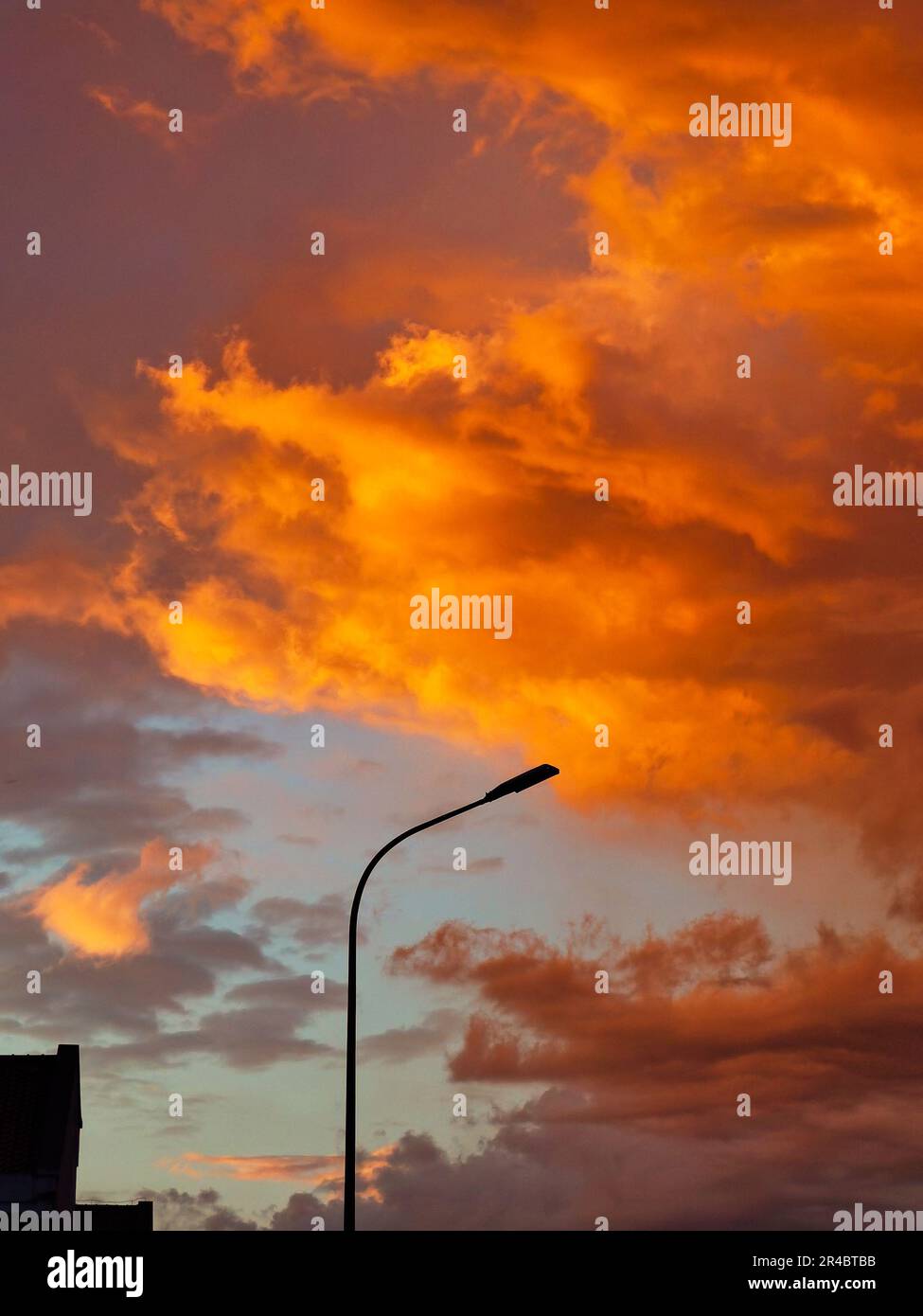 A street lamp stands silhouetted against a vibrant sunset sky ...