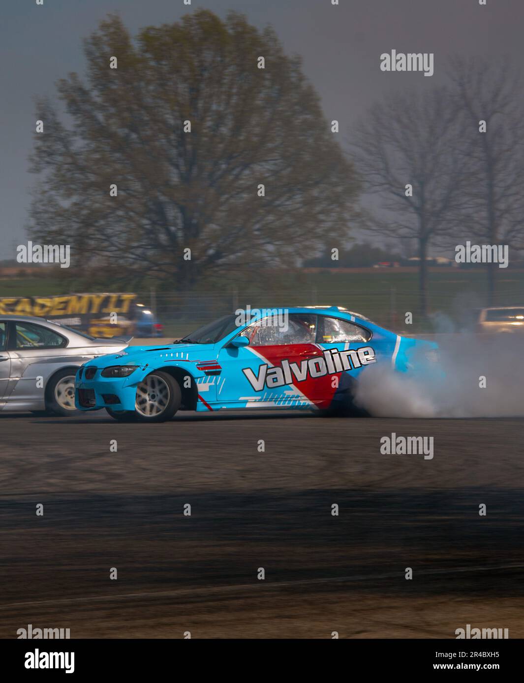 Two cars speeding around an auto race track, with smoke billowing in ...