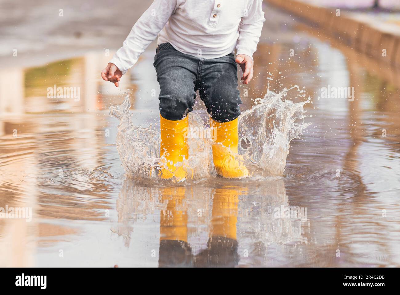 A child's feet in yellow rubber boots jumping over a puddle in the rain ...