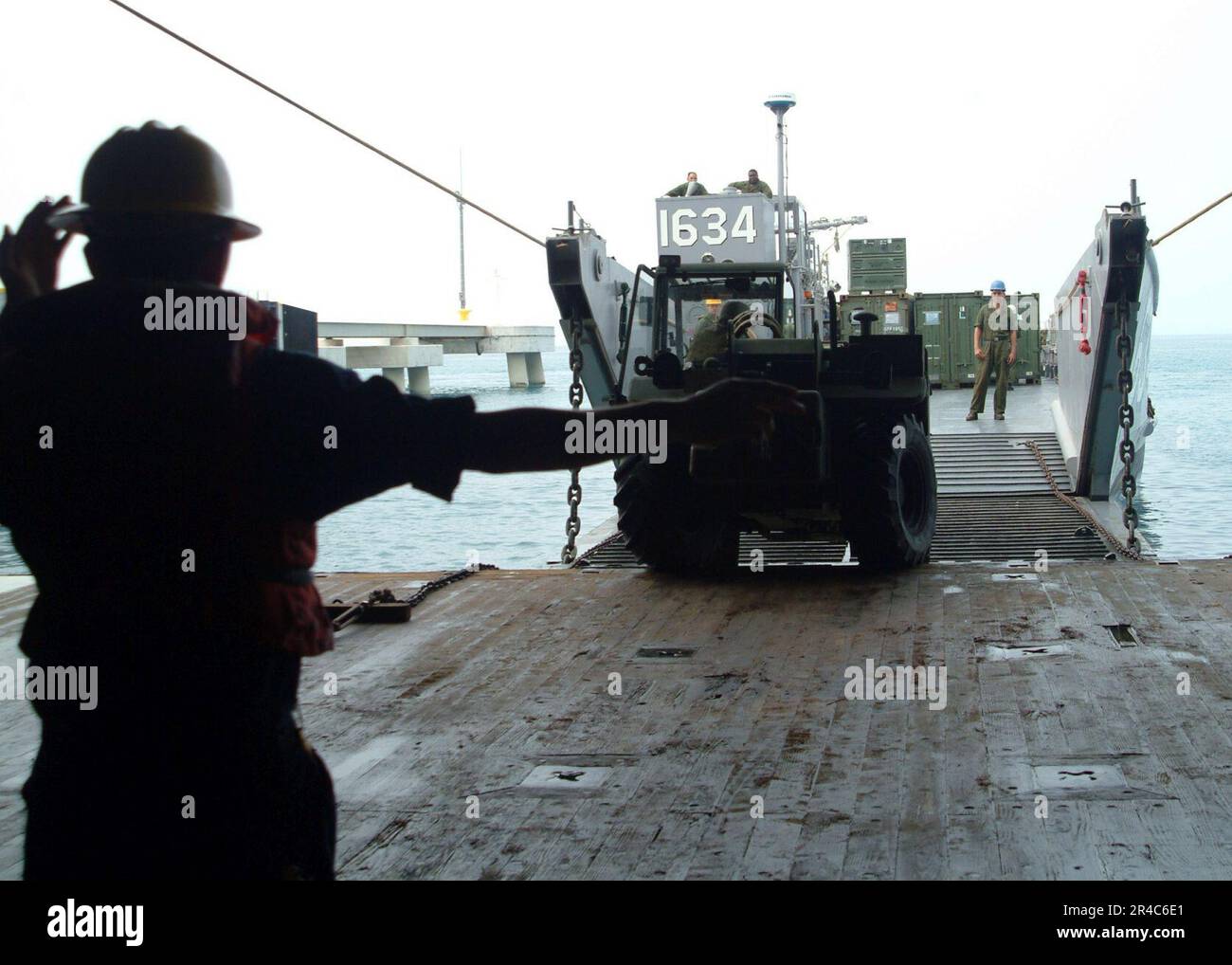 US Navy Boatswain's Mate 2nd Class guides a Marine forklift on to the ...