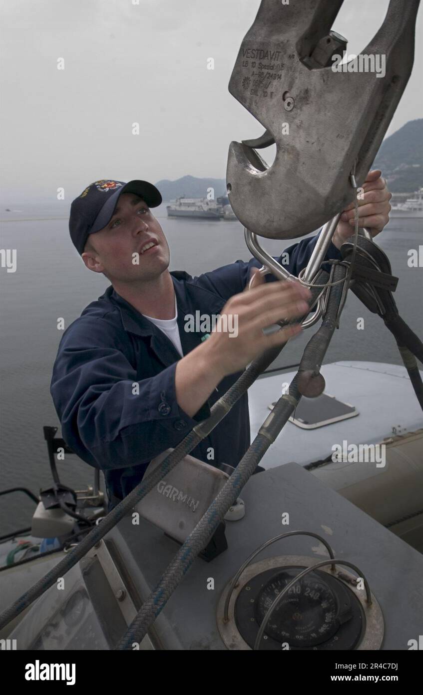 US Navy Seaman attaches a Rigid Hull Inflatable Boat to a davit crane ...