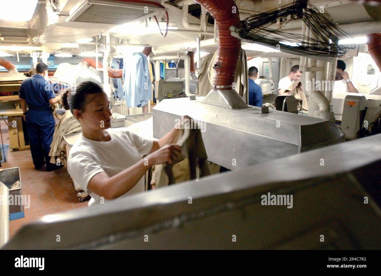 US Navy Airman prepares to press a uniform in the ship's laundry aboard ...