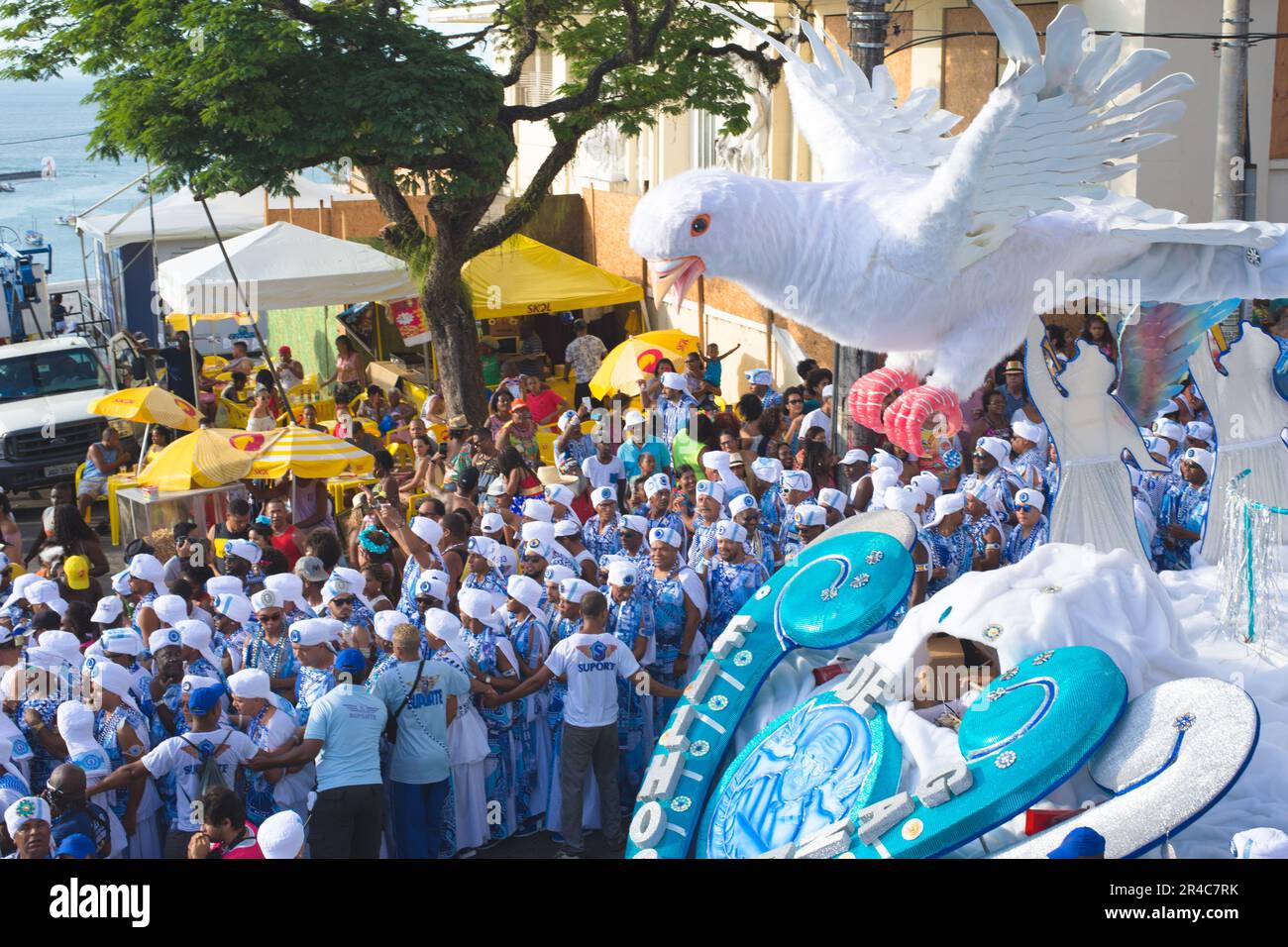 A diverse crowd of people stands in a street watching a vibrant float ...