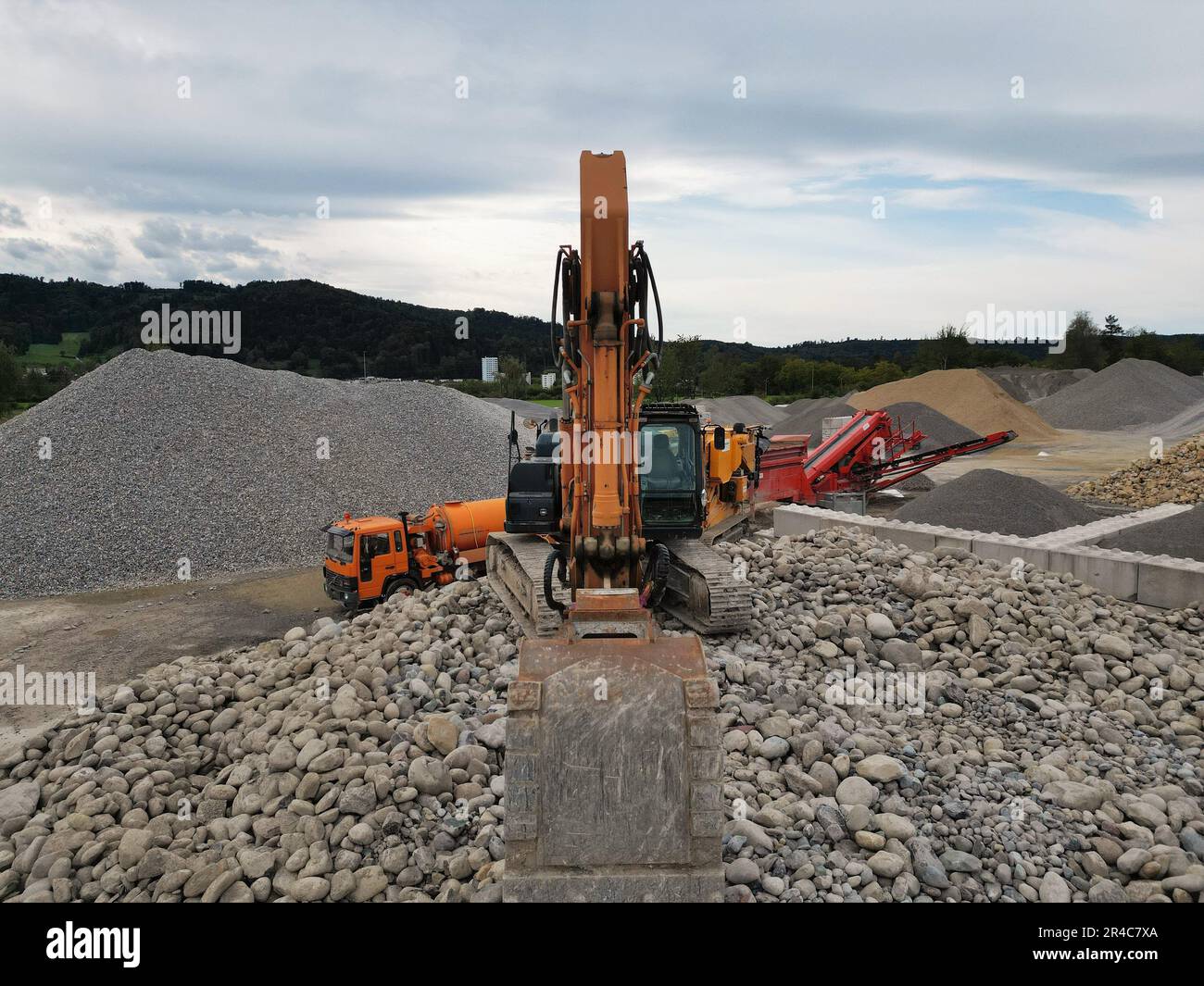 Two large excavators are positioned in a large gravel yard in an open ...