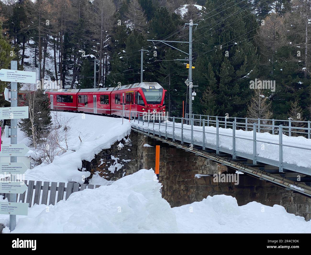 A bright red train passes over a steel bridge with snow dusted on the ...