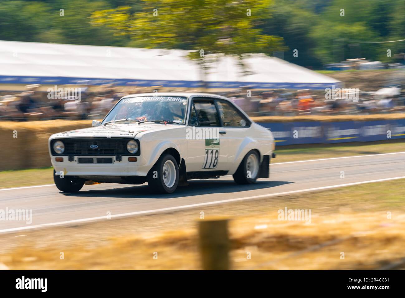 A Caucasian male drives a white sedan down a road surrounded by a rural ...