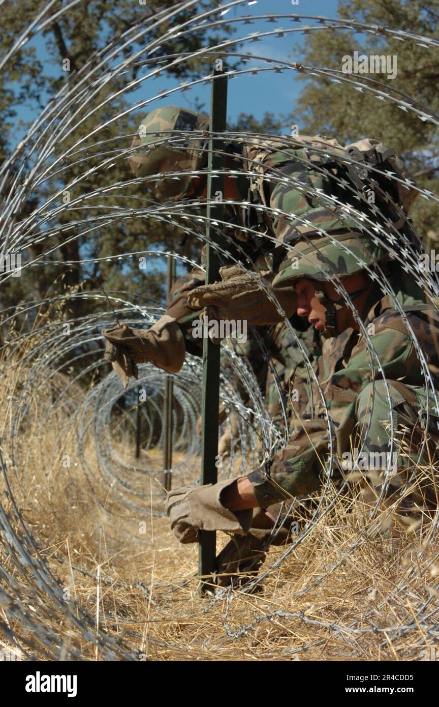 US Navy Builder 3rd Class Antonio a strand of barbwire to a stake to ...