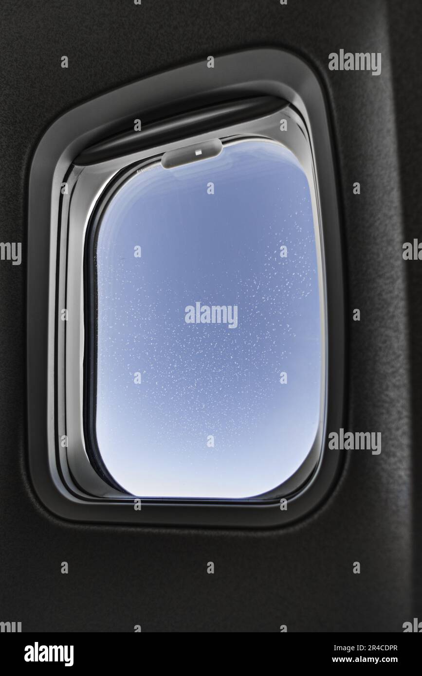 Small typical airplane window with some ice on the surface of the glass ...