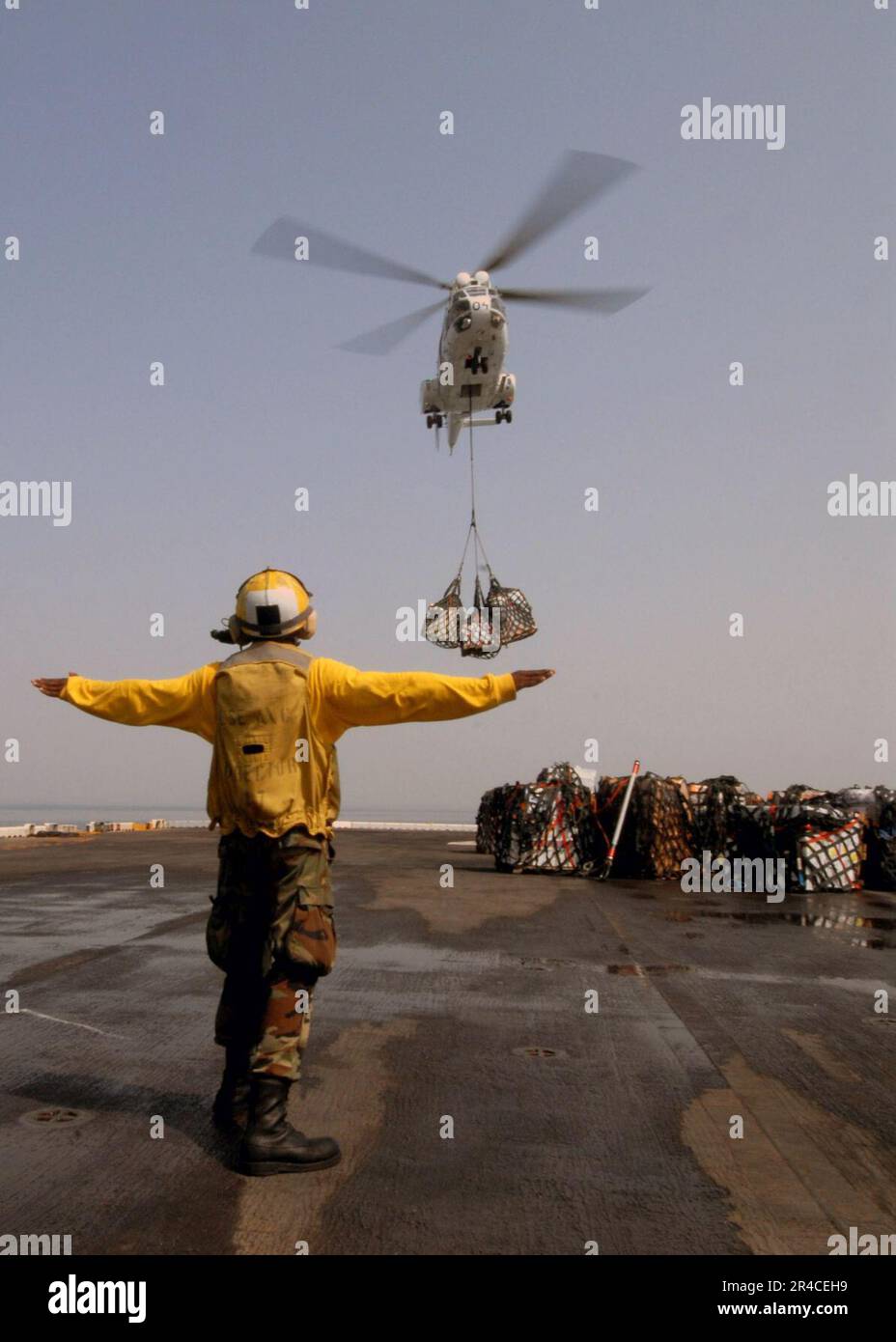 US Navy A sailor on the flight deck directs a helicopter loaded with ...