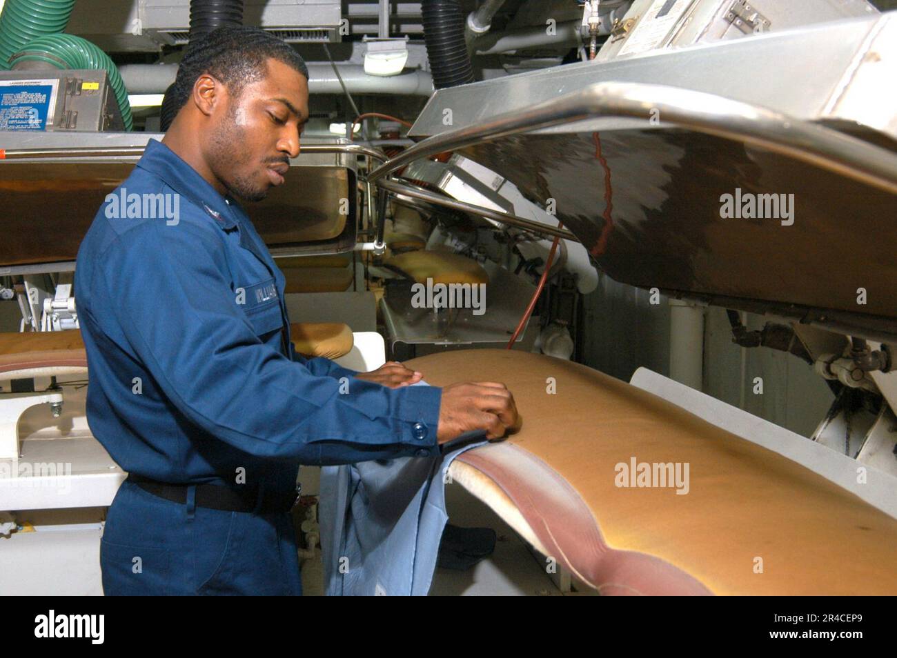 US Navy Ship's Serviceman presses a utility uniform in the ship's ...