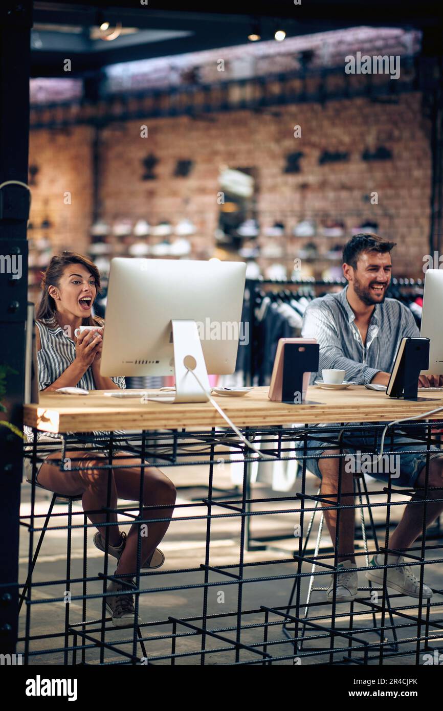 Two workers in a clothing store working at the desk, sitting in front ...