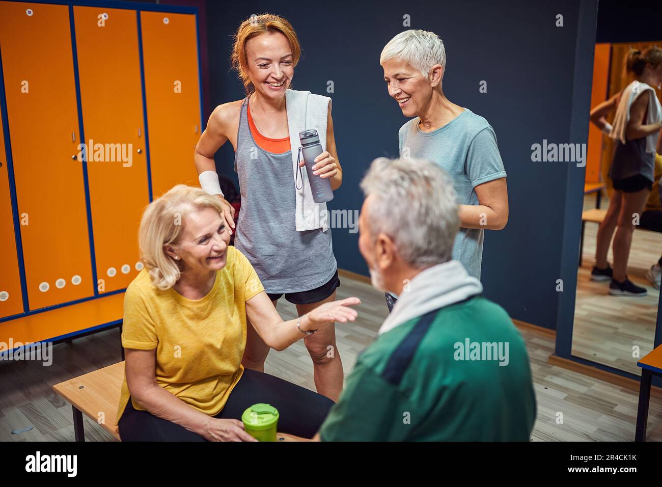 Senior man and women with young woman trainer in gym locker room before ...