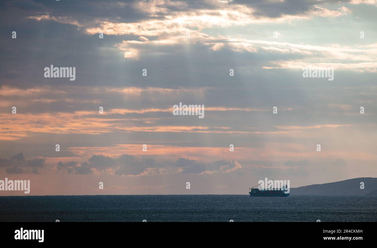 Seascape. Sunbeam through cloud colors sky, silhouette of line ship as ...
