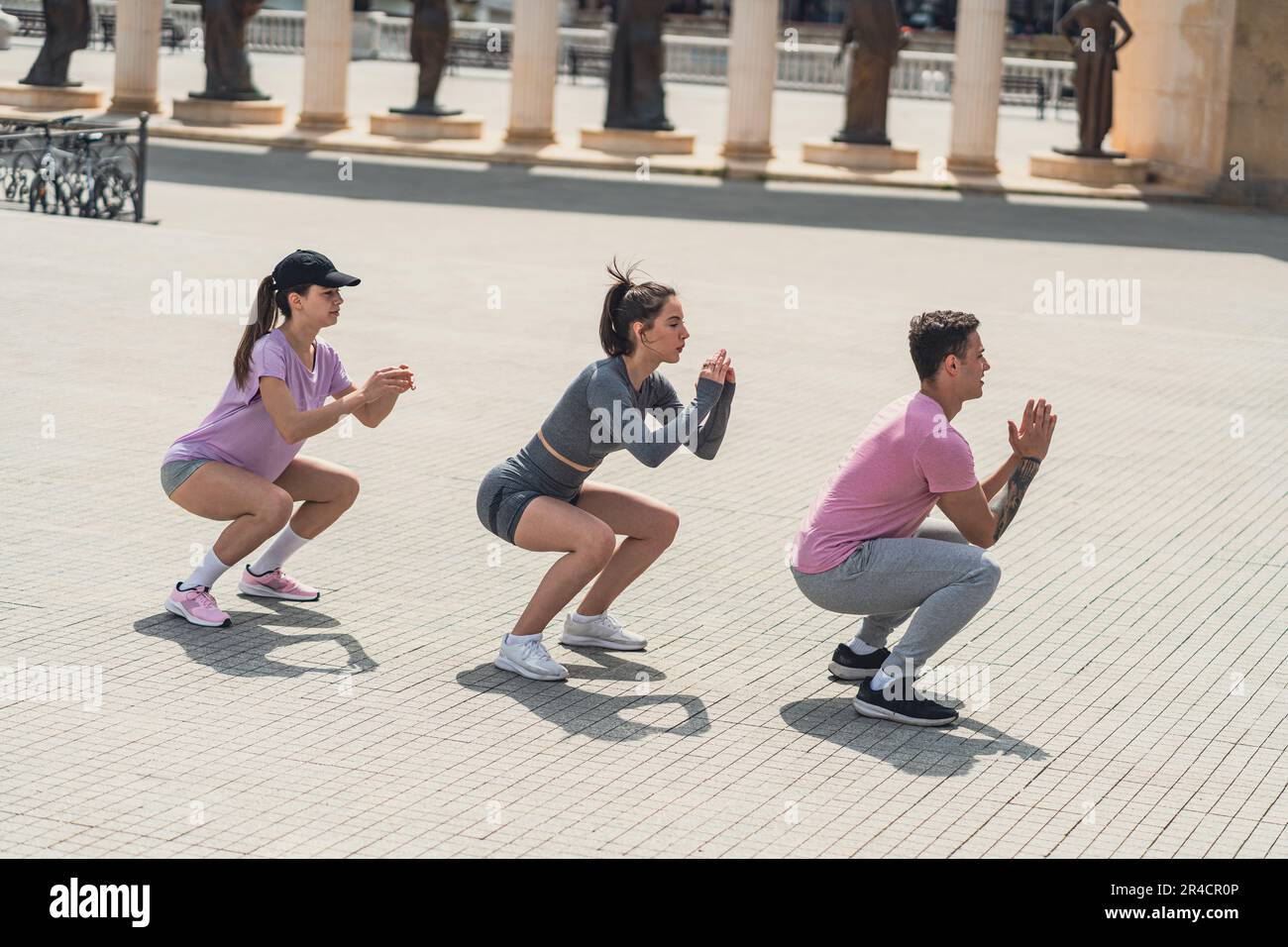 Workout in the city. Three fit friends doing squats. Side view shot ...