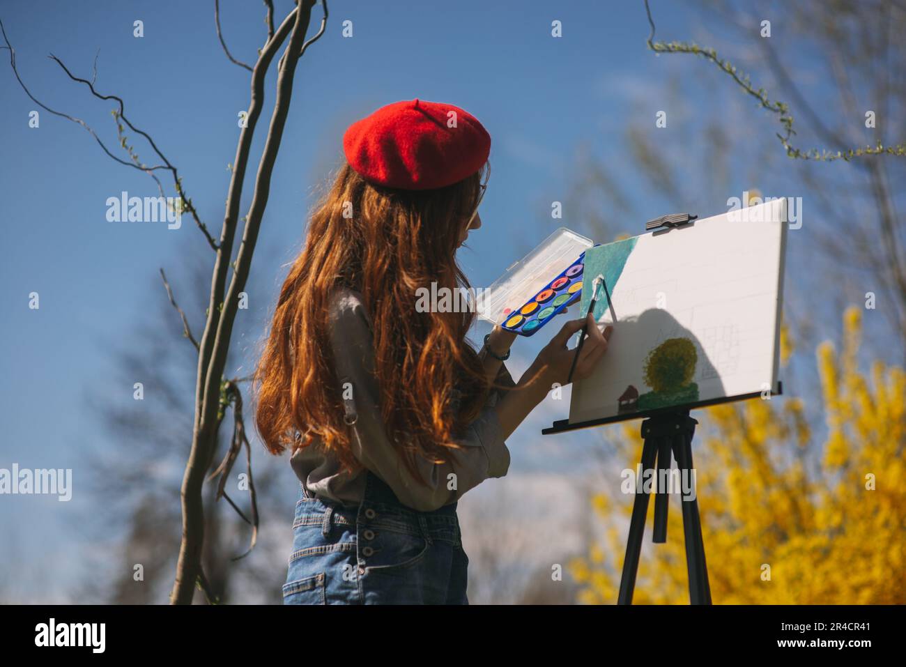 Beautiful ginger female artist painting a canvas on an easel with a ...