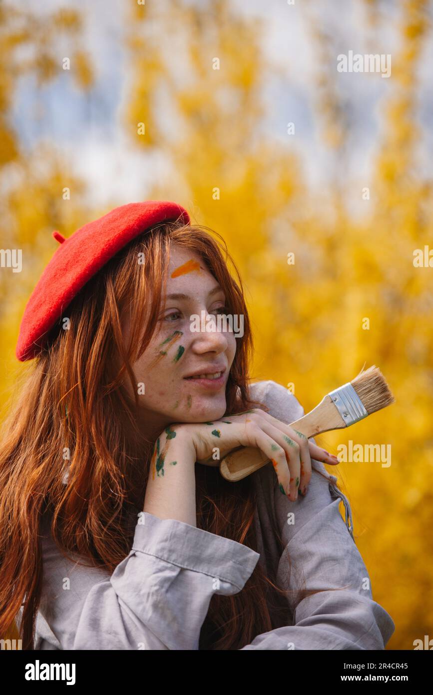 Portrait of beautiful ginger girl painter posing with her big brush ...