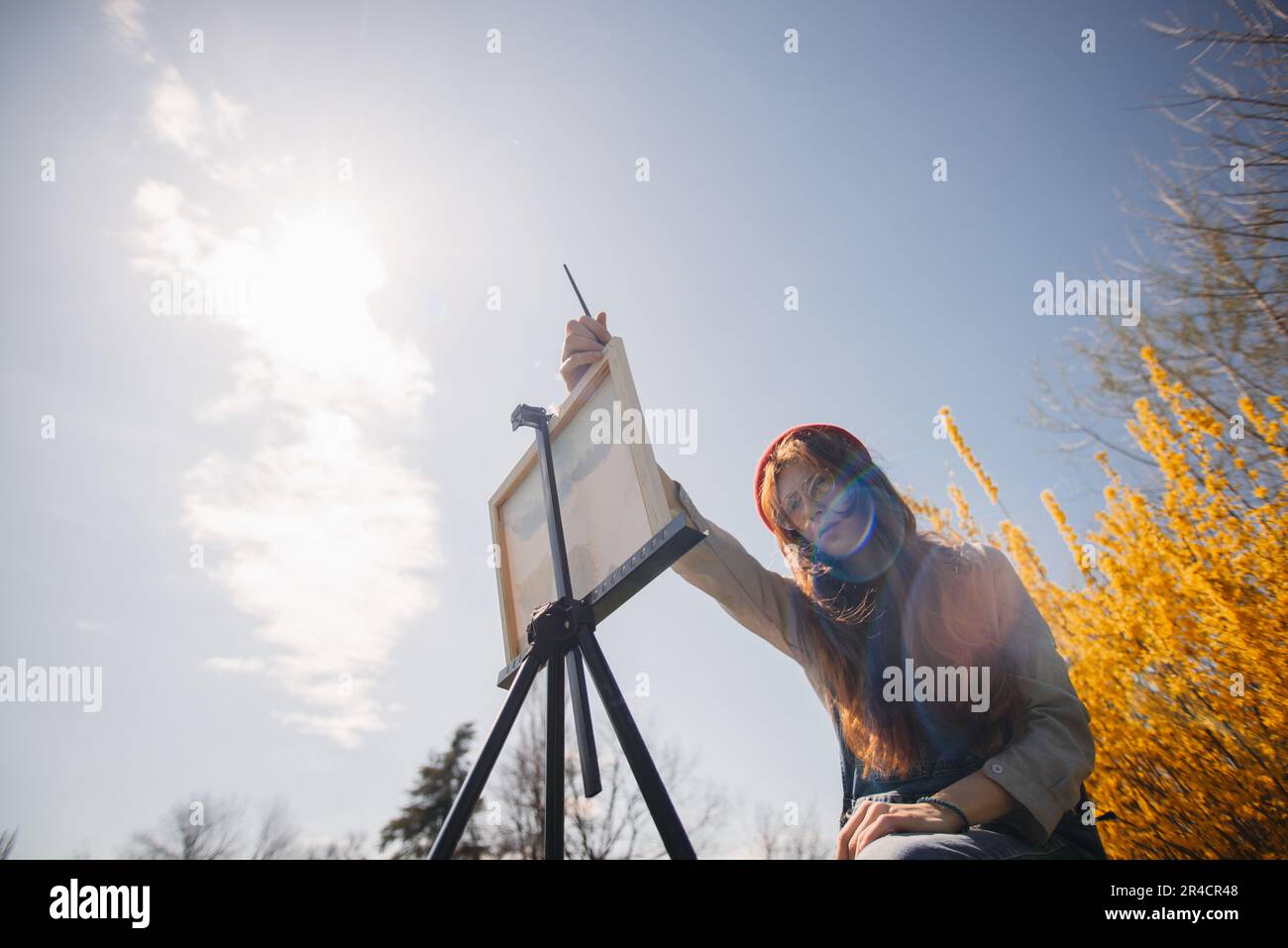 Female ginger artist painting while sitting in nature at the park in ...