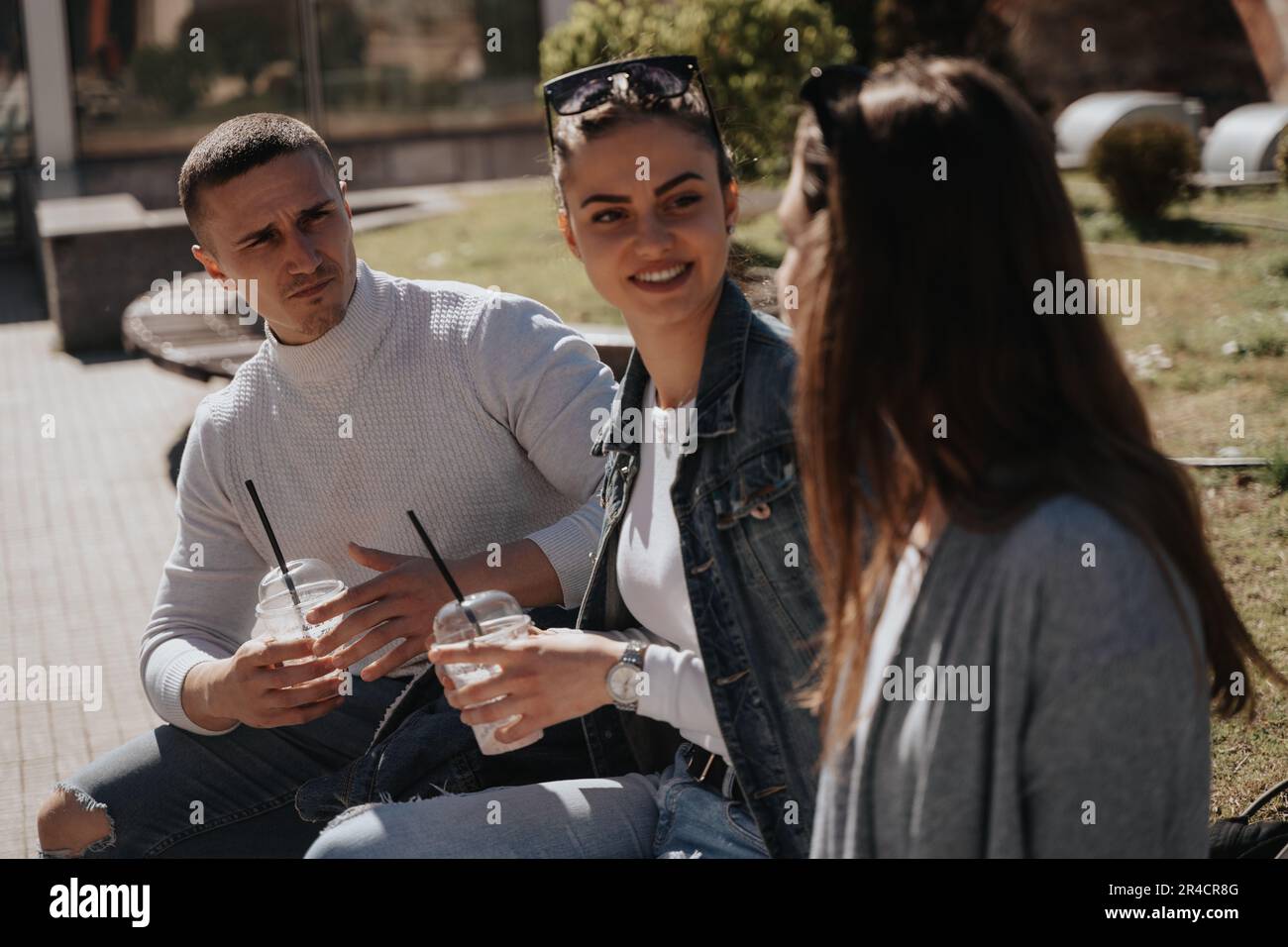Three best friends talking while sitting and holding milkshake cups at ...