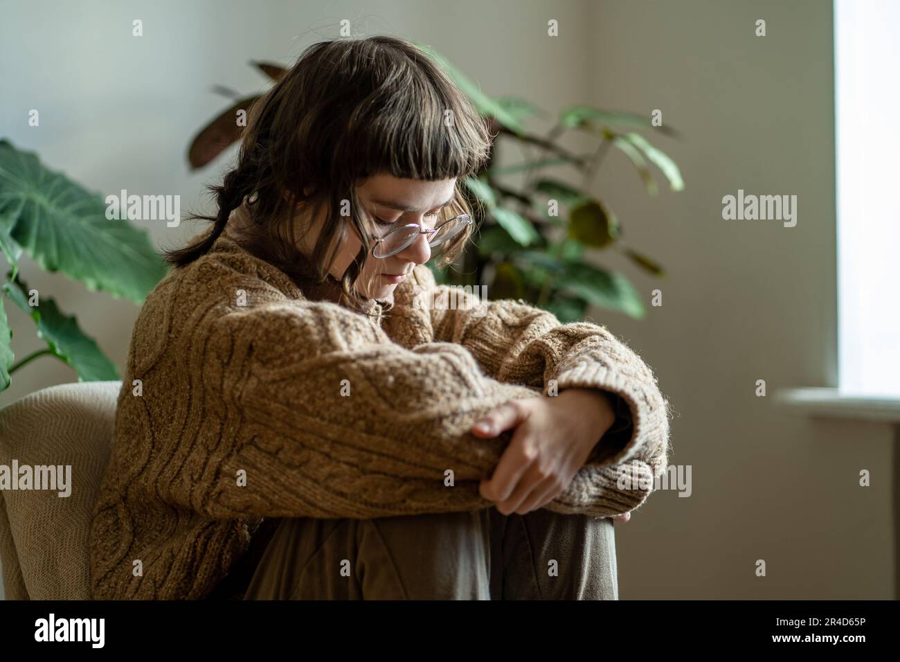 Sad millennial girl artist sitting on chair by window feeling lack of ...