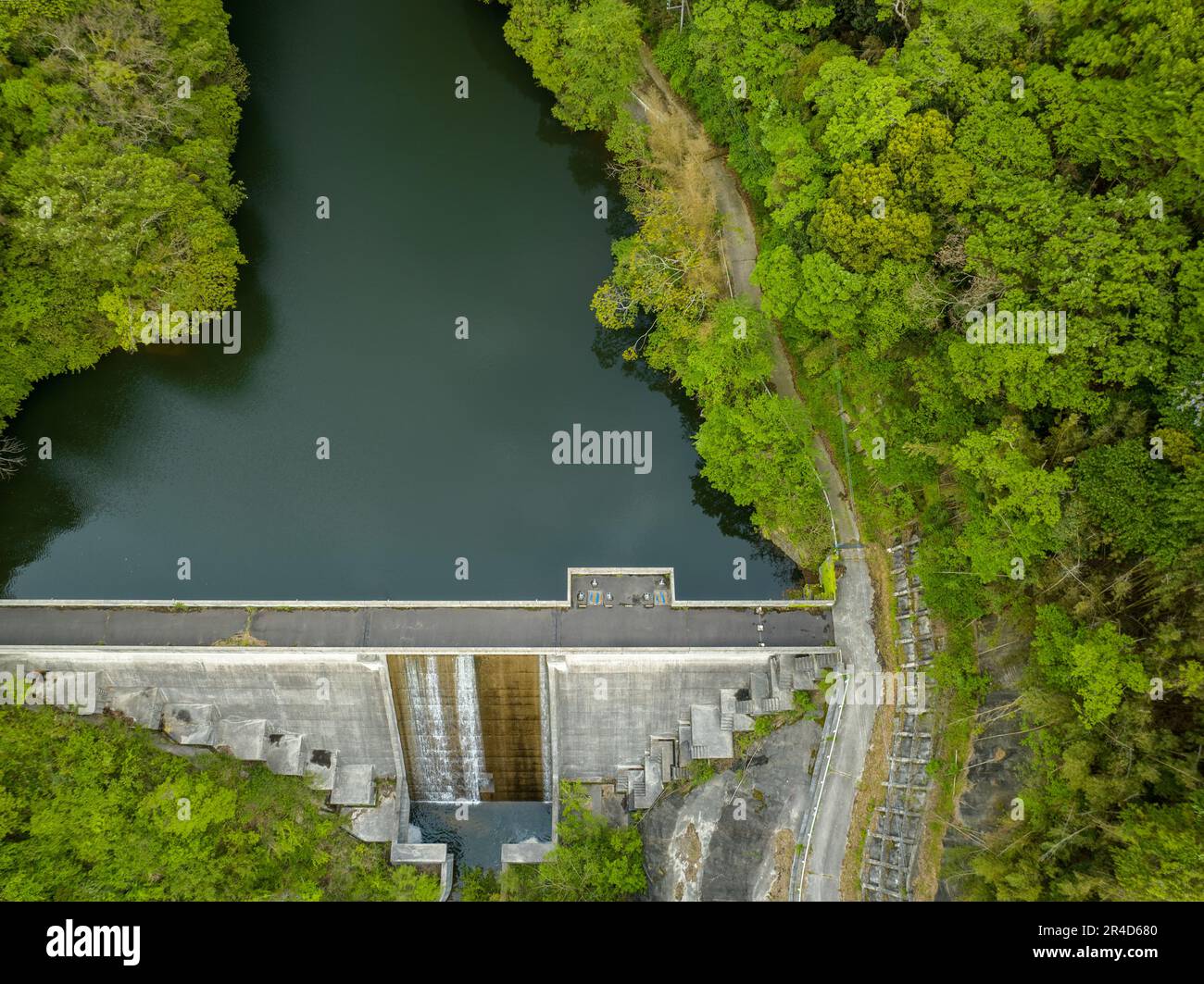 Small dam holds back water in storage reservoir surrounded by trees ...