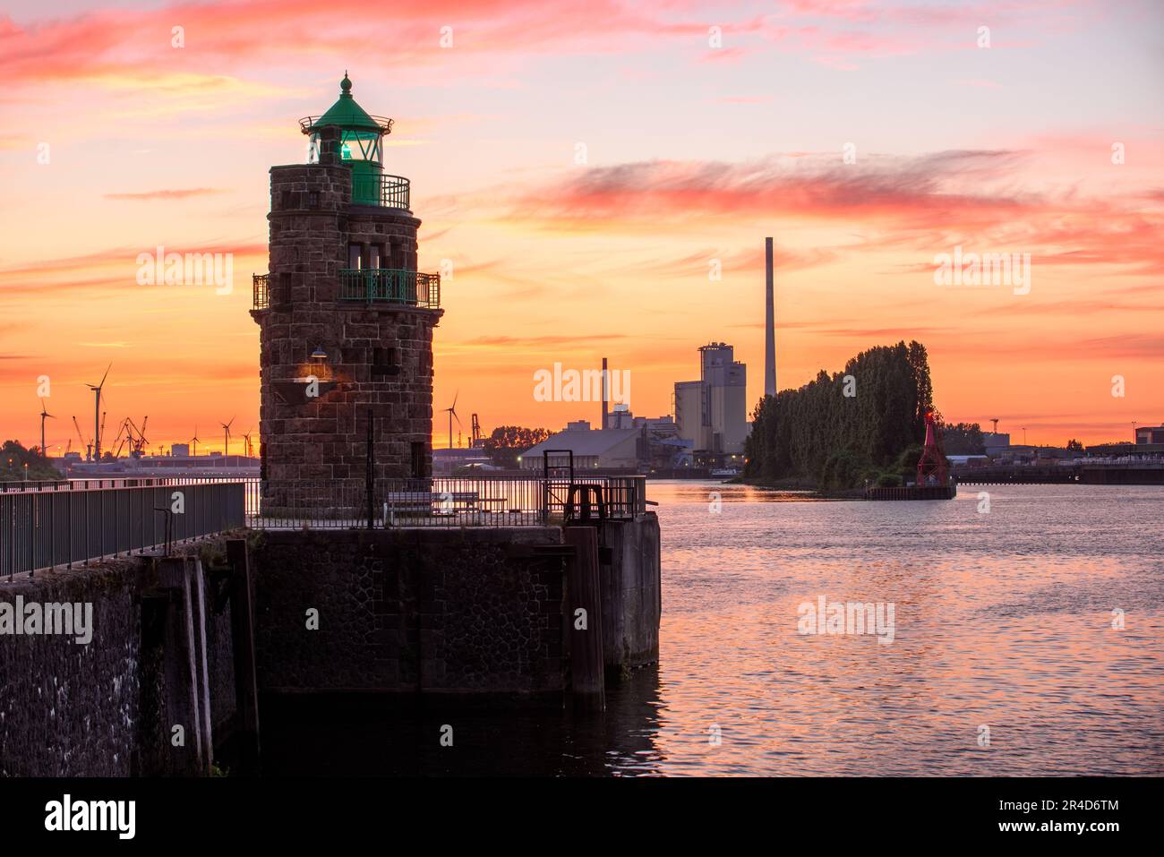 Historic lighthouse on a river harbour at sunset. Industrial buildings ...