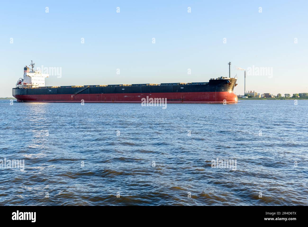 Large bulk carrier ship leaving a river harbour at sunset in summer ...