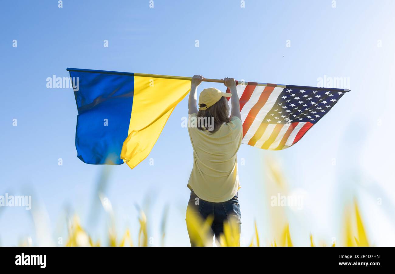 woman on sunny day stands with back and raises up two large flags ...