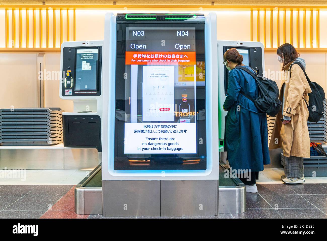 Check-in baggage machine with 2 women checking-in using the luggage tag ...