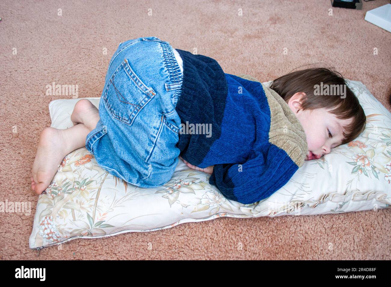 Child, boy, one year old, laying asleep on a cushion on the floor. Typical infant sleeping ...