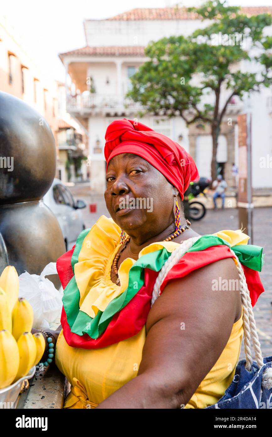 A colorfully dressed Cartagenaro woman fruit vendor looks at the camera ...