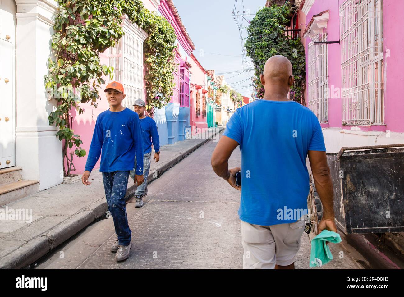 Men walk past each other on a street with bright pink buildings in ...