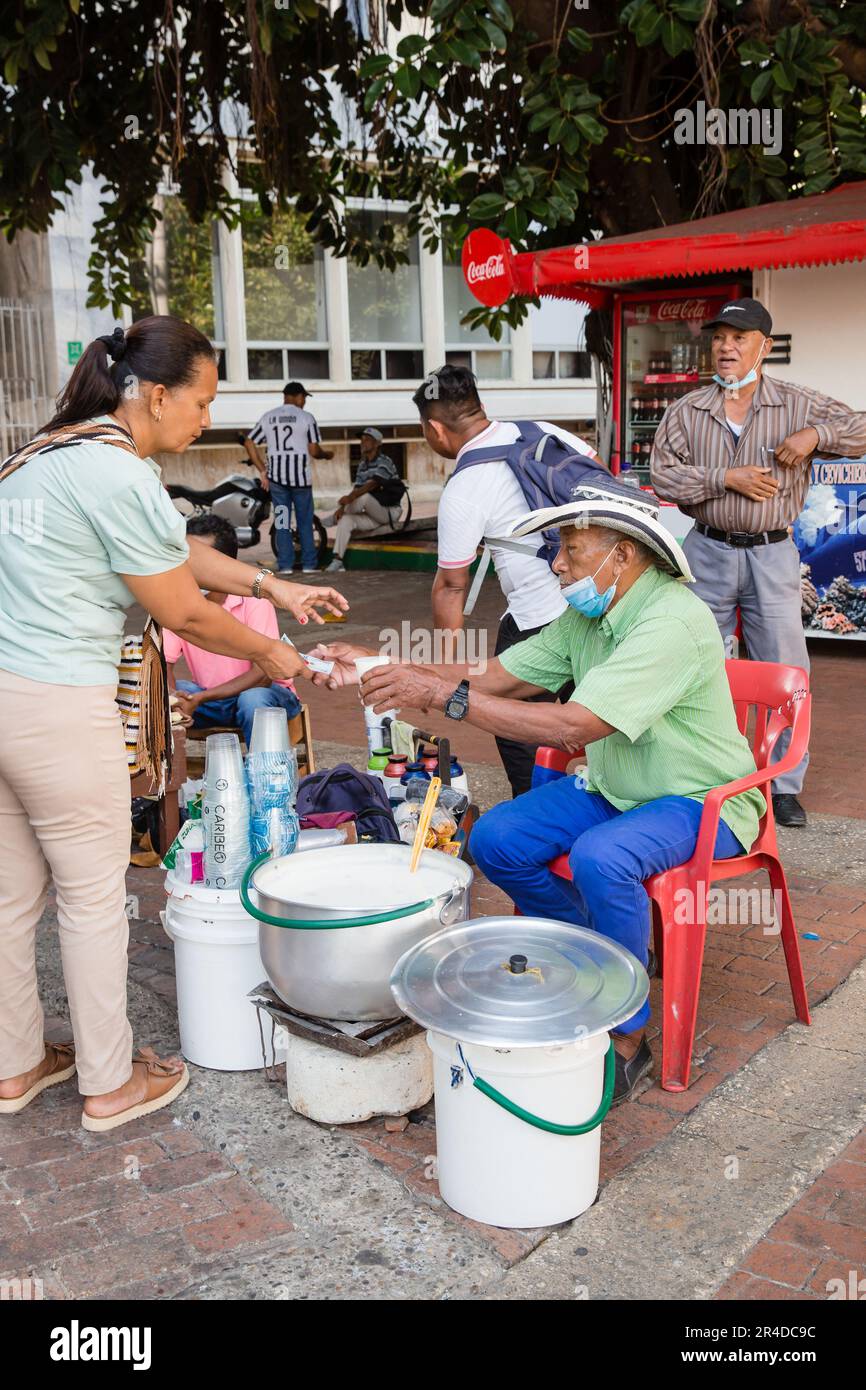 A Cartagnero street food vendor sits on a busy corner and helps a ...