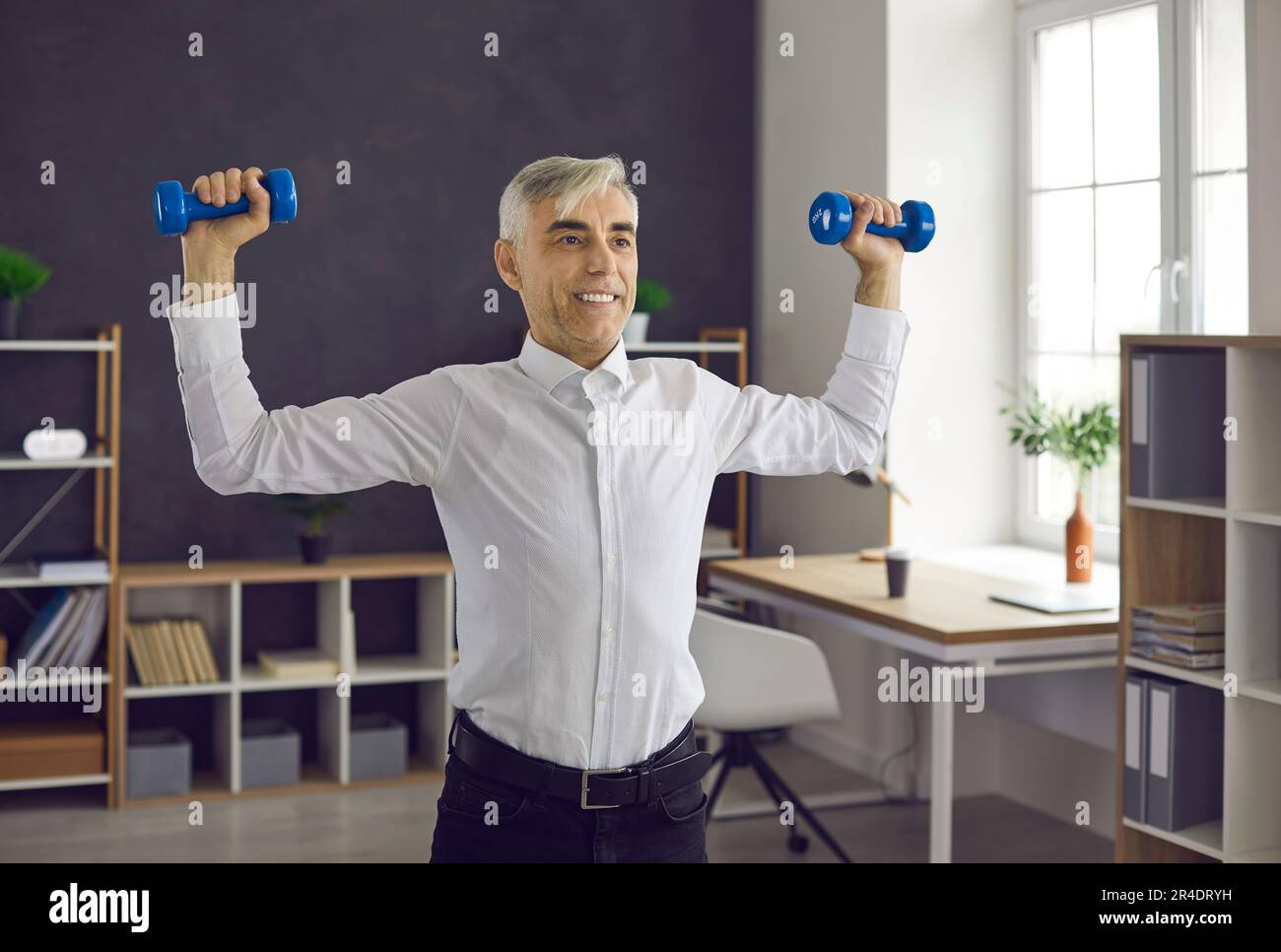 Happy senior worker doing fitness exercise during working day in office ...