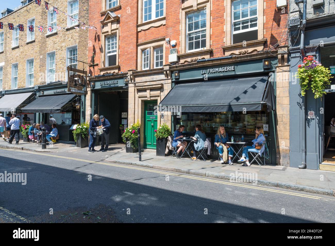 People seated at pavement tables at La Fromagerie enjoy food and drink ...