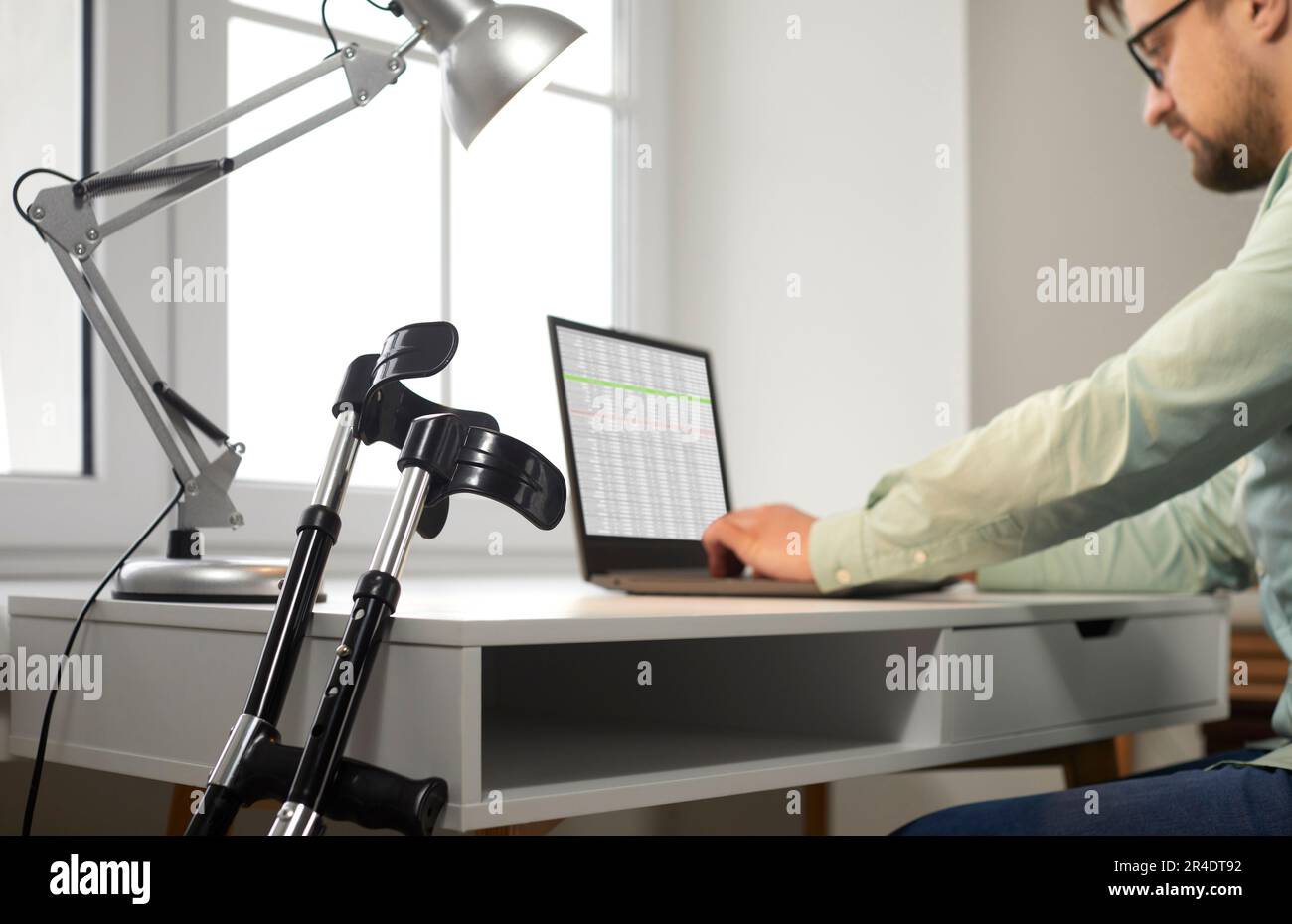 Crutches by office desk with disabled man working in laptop computer in ...