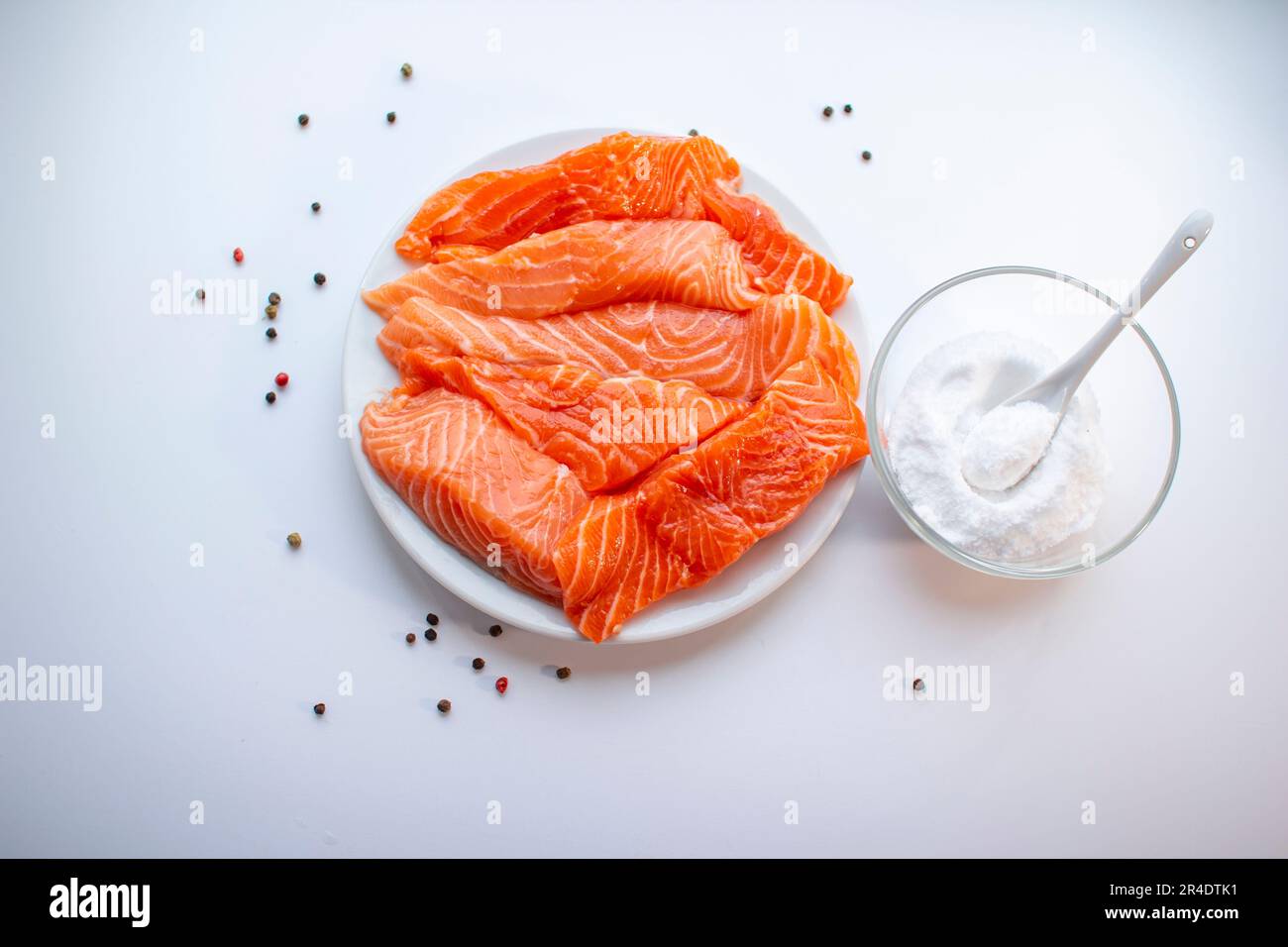 Fresh raw salmon fish fillet on a white plate, a small bowl of salt and ...