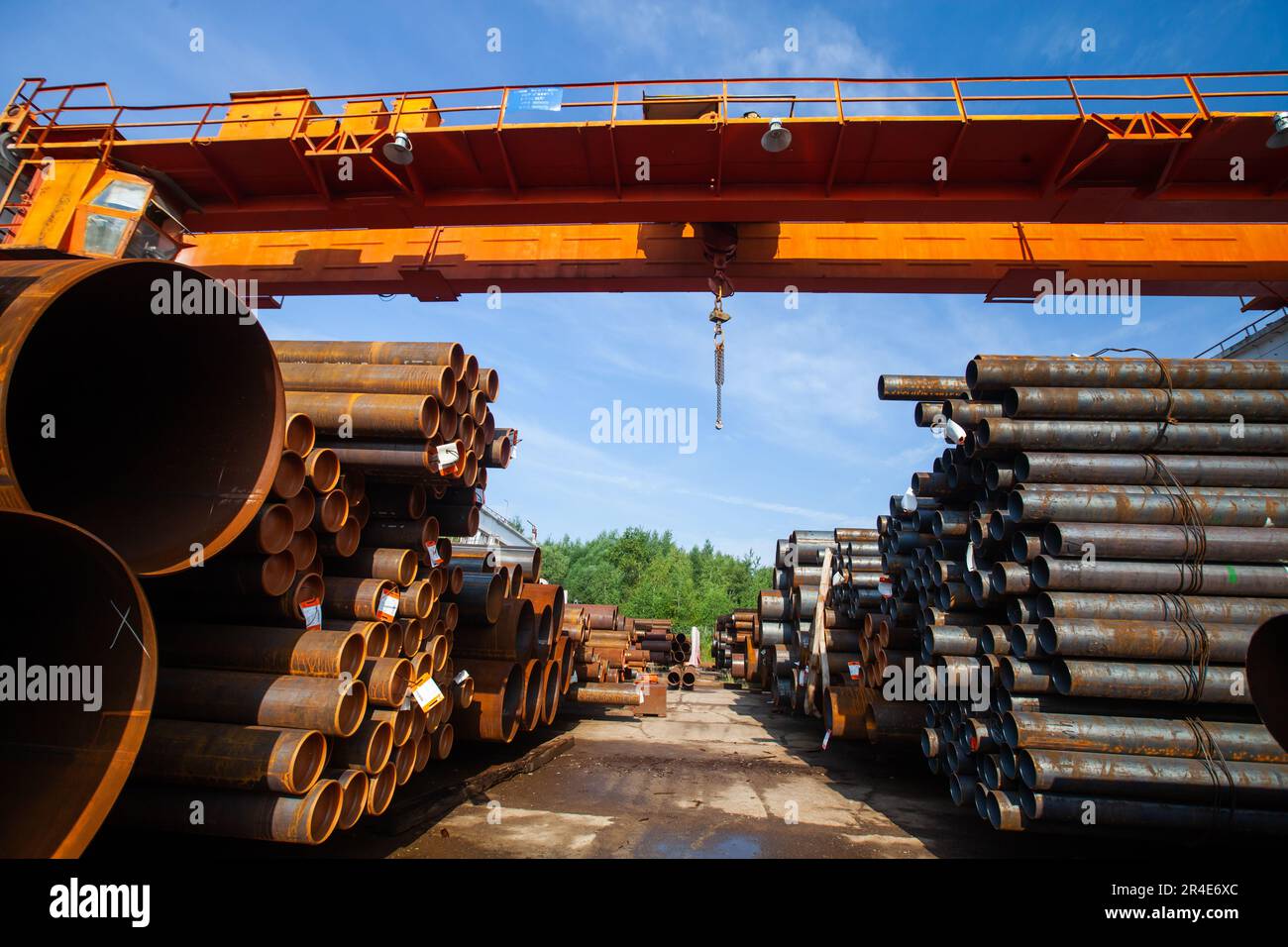 Stack of steel pipes outdoor warehouse. Bridge crane on blue sky ...