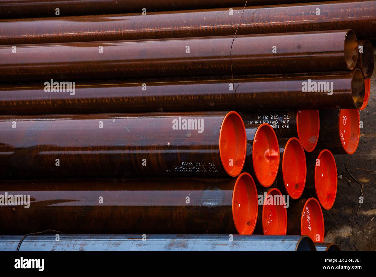 Wet steel rusty pipes with red plastic caps on outdoor warehouse in ...